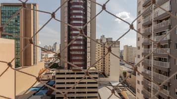 Um edifício alto com vários andares, cercado por outros edifícios, visto através de uma grade de arame.