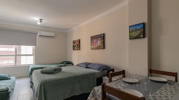 Quarto com duas camas, uma mesa de jantar e cadeiras, e uma janela com vista para edifícios.
