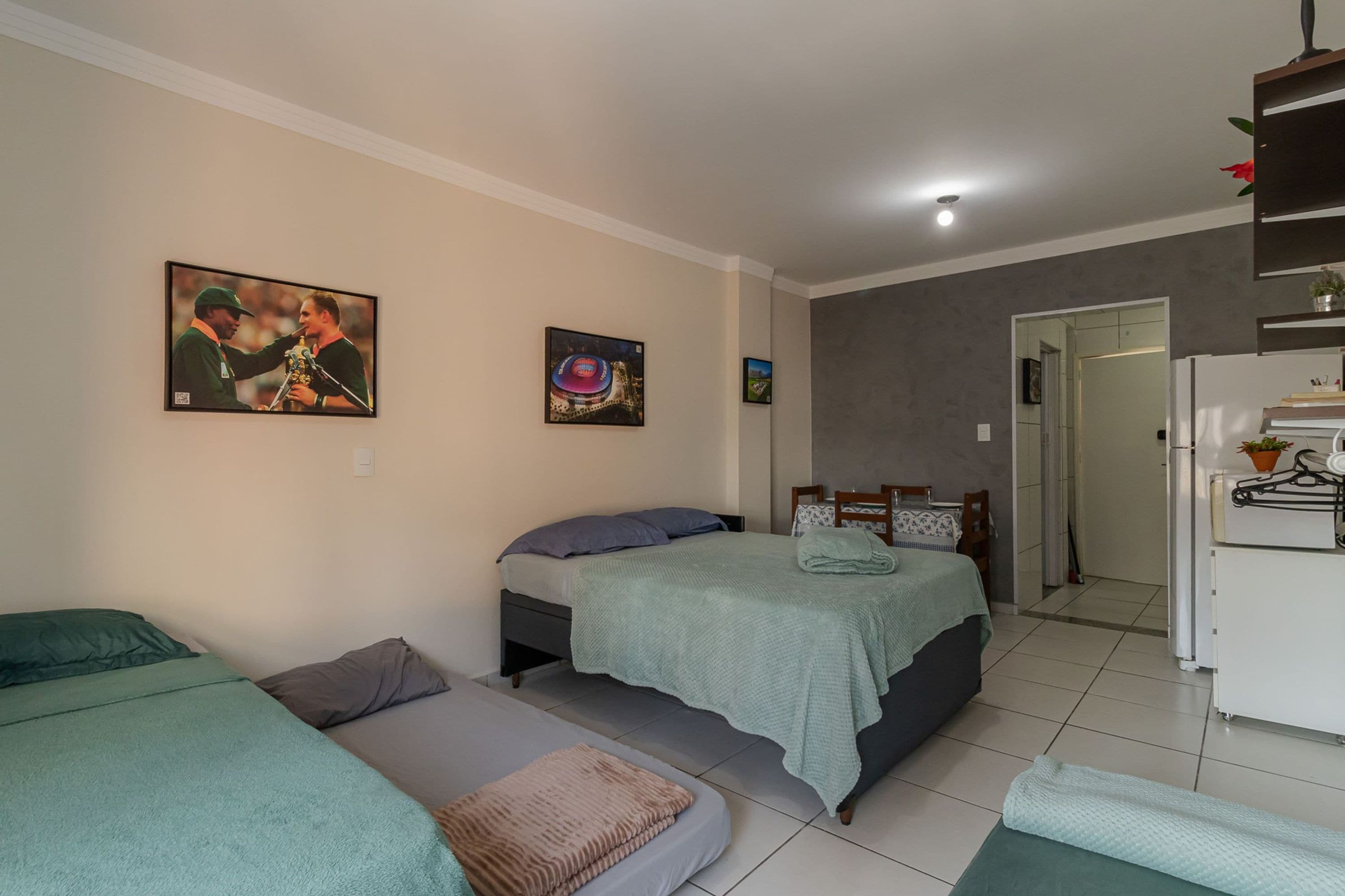 Quarto com duas camas, uma mesinha e um frigorífico.