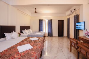 Quarto de hotel com duas camas, televisão, escrivaninha e porta do banheiro.