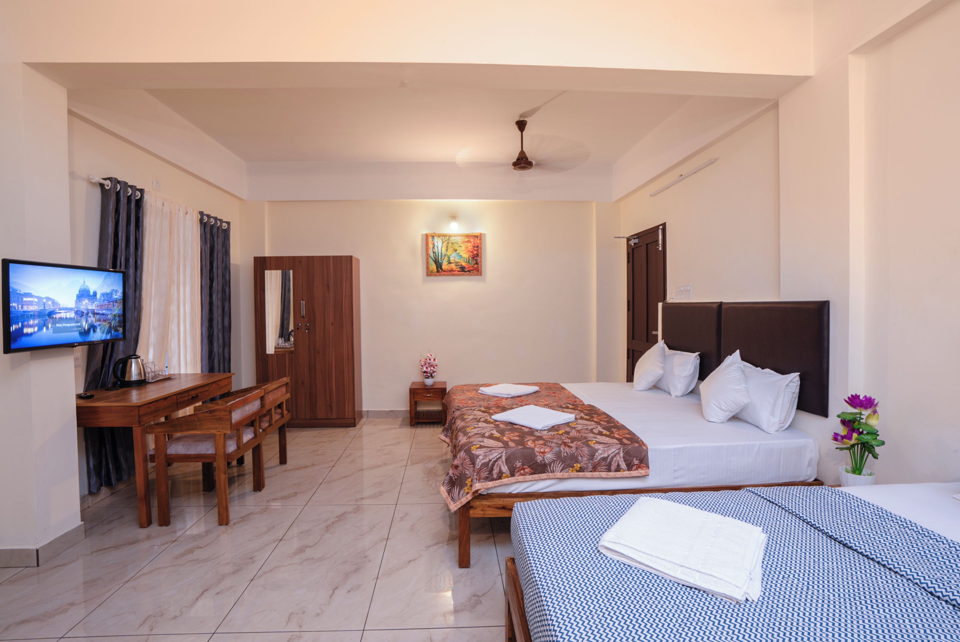 Quarto de hotel com uma cama, escrivaninha, televisão e um quadro na parede.