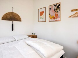 Quarto com cama, mesa de cabeceira, ventilador de teto e duas obras de arte emolduradas na parede.