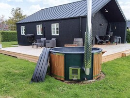 Uma banheira de hidromassagem moderna ao ar livre, com revestimento de madeira, um deck com mobiliário externo e um edifício grande ao fundo.