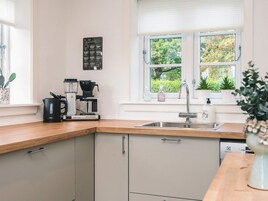Cozinha com máquina de café, pia e janela com vista para o verde.
