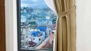 Janela com vista para uma área residencial, cortinas entreabertas e chão de madeira.