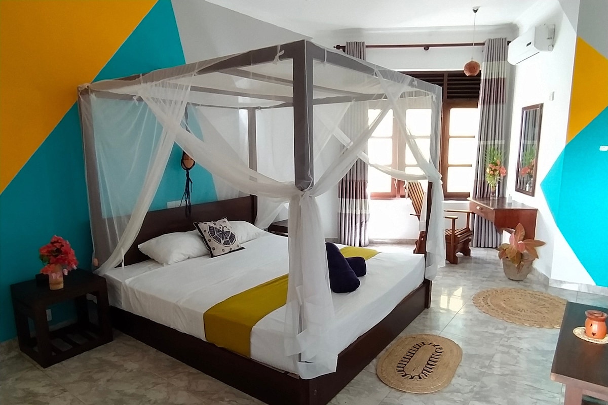 Uma cama com dossel, uma mesinha de cabeceira com um vaso e vista para o exterior.