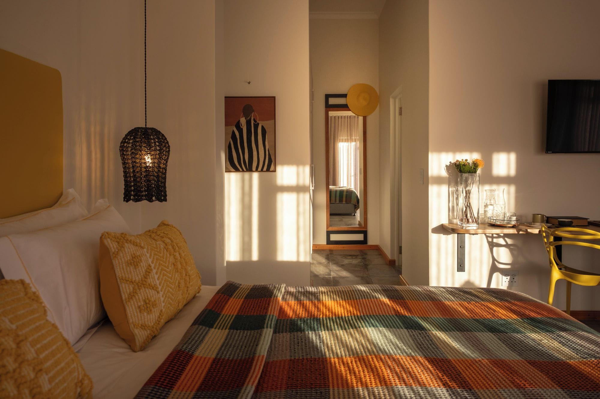 Quarto de hotel com cama, escrivaninha, cadeira e vista para o corredor.