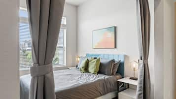 Quarto com cama, almofadas, mesa de cabeceira, abajur e um quadro na parede.