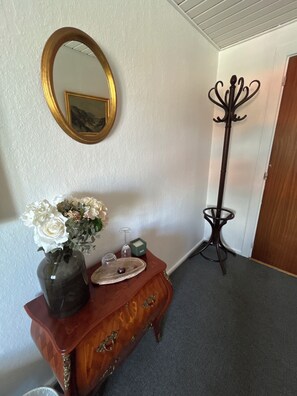 Uma cômoda de madeira com um vaso de flores, um espelho e um tabuleiro com um copo e uma vela.