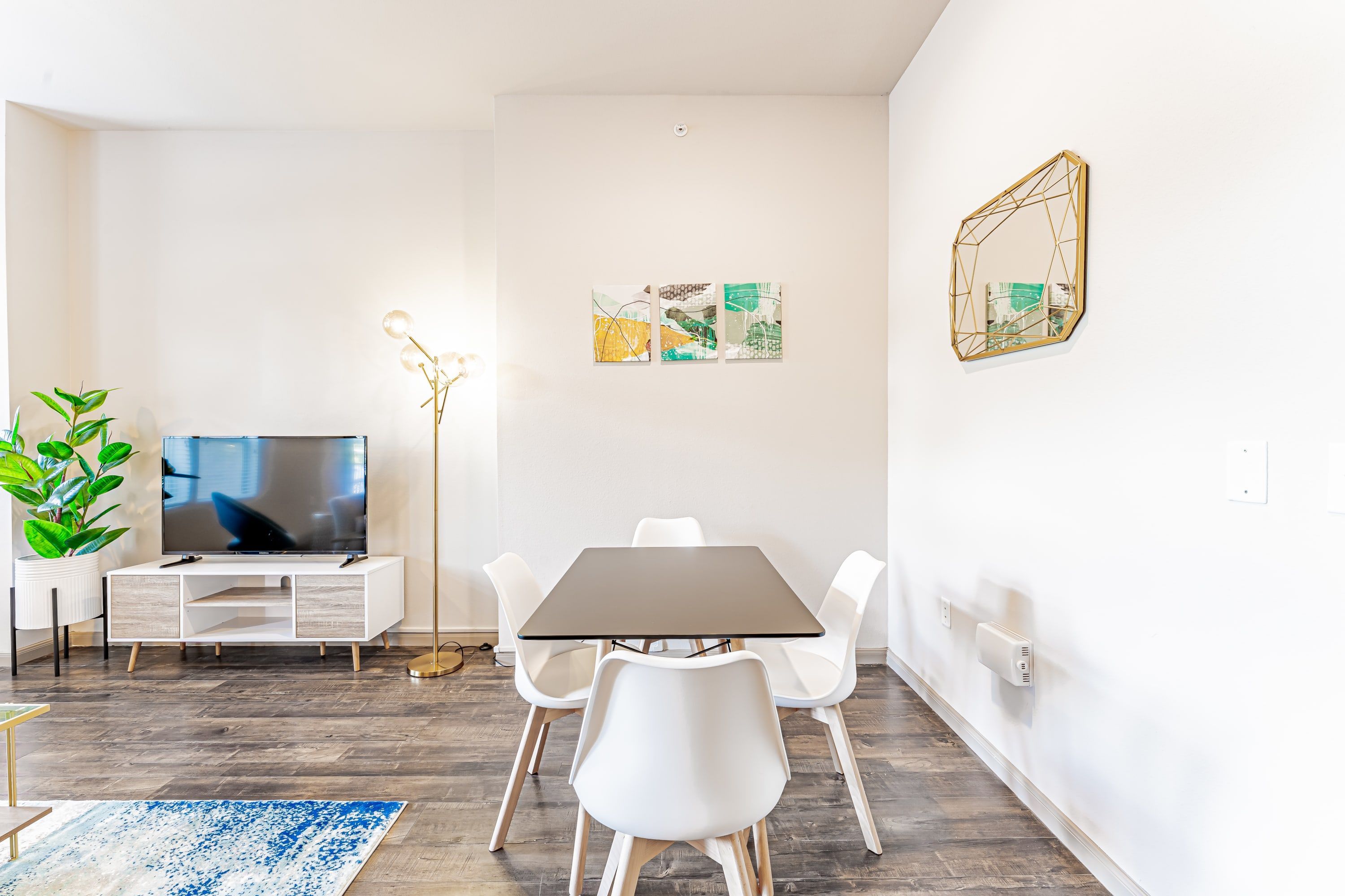 Sala de estar moderna com televisão de tela plana, mesa de jantar com cadeiras, abajur e obras de arte na parede.