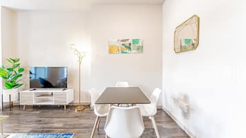 Sala de estar moderna com televisão de tela plana, mesa de jantar com cadeiras, abajur e obras de arte na parede.