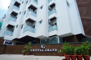 Um edifício com vários andares, um letreiro com a inscrição 'KRISTAL GRAND' e varandas com aparelhos de ar condicionado.