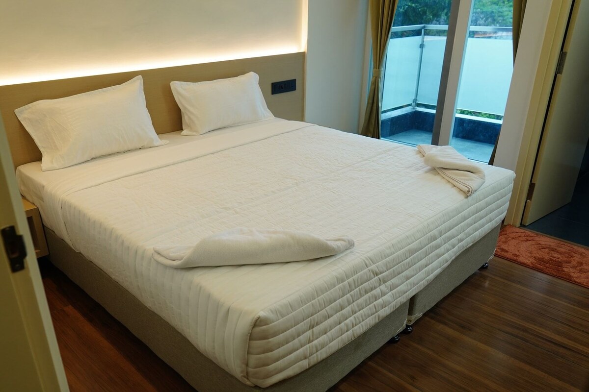 Quarto de hotel com cama grande, cabeceira e vista para o exterior através de uma porta deslizante.