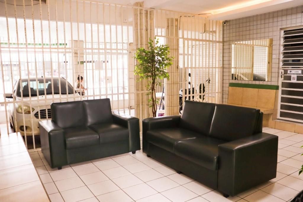 Quarto com sofá de couro preto, piso de azulejos brancos e uma grande janela com vista para um carro do lado de fora.