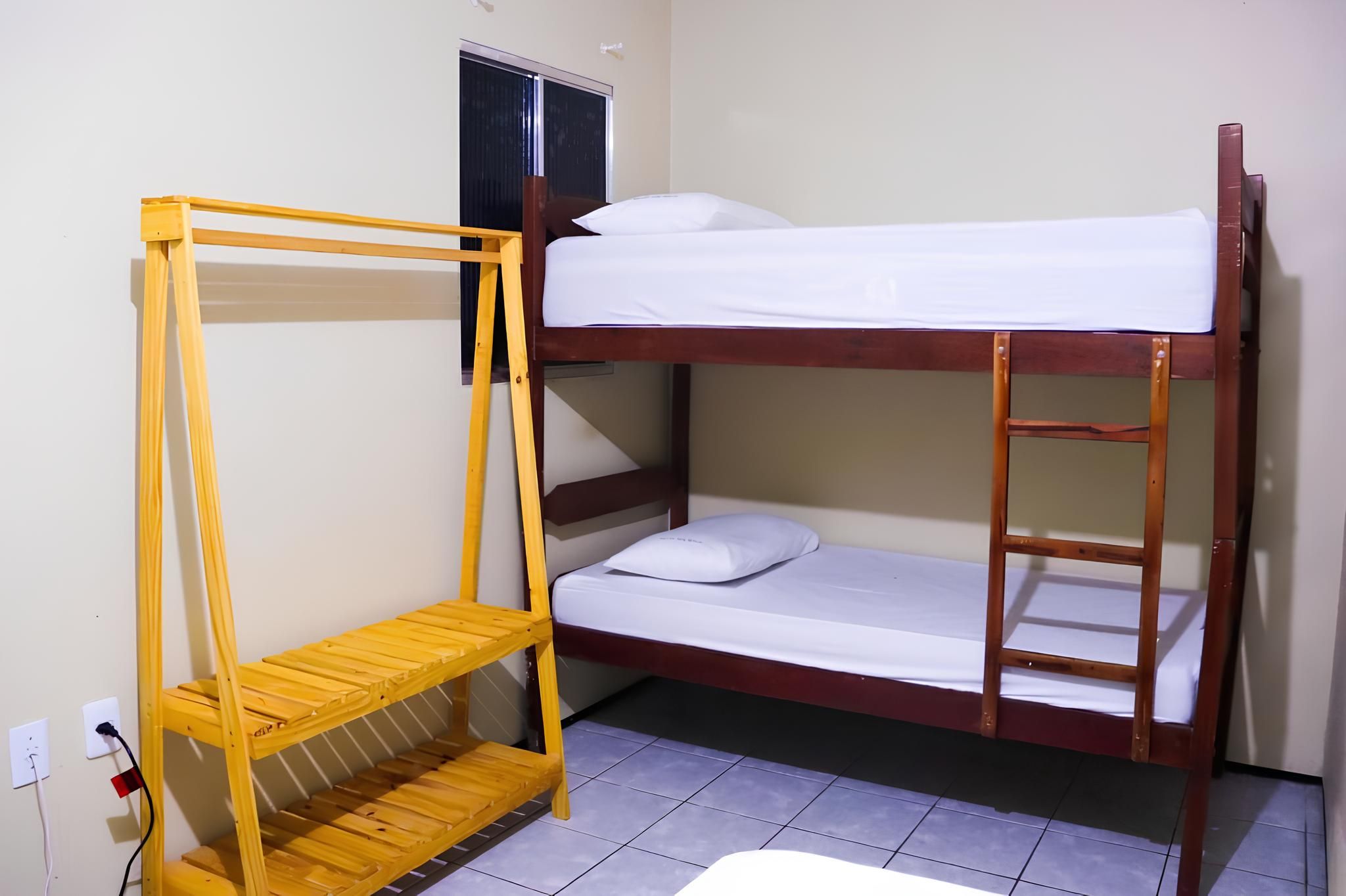 Uma cama beliche com escada de madeira, prateleira, janela e tomada.