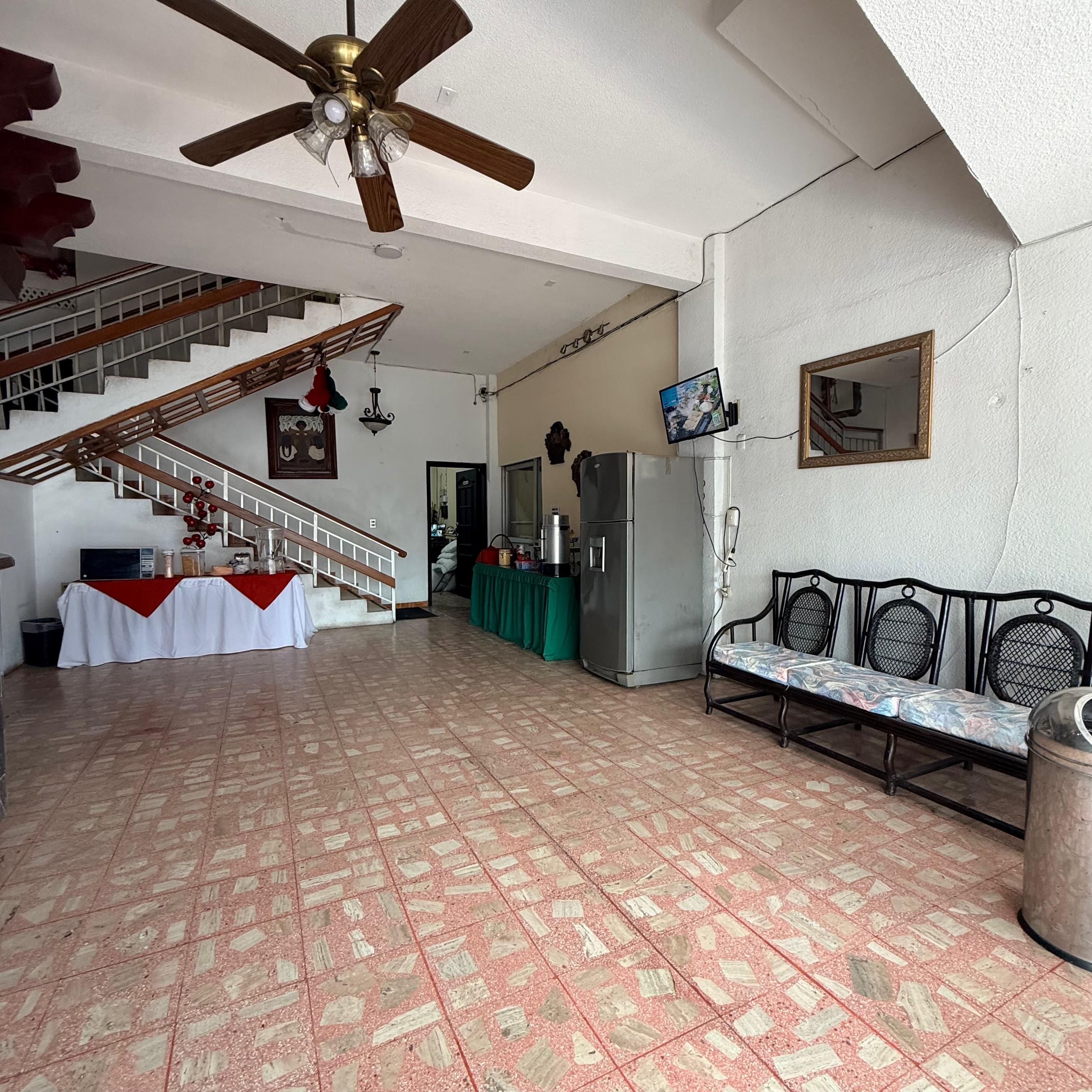 Um quarto espaçoso com piso em azulejo, ventilador de teto, escada, geladeira, um banco e uma televisão fixada na parede.