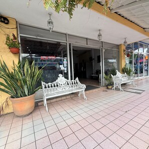 Entrada de um edifício com um banco, plantas em vasos e uma placa que diz 'ABIERTO'.