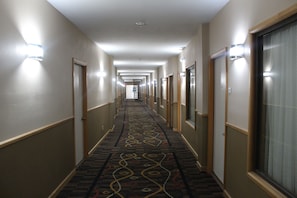 Um corredor de hotel com pisos cobertos de carpete, portas em ambos os lados e luminárias nas paredes.