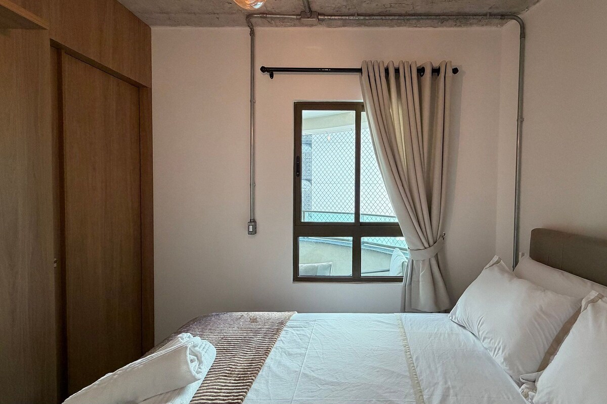 Quarto com cama, janela com cortinas e porta.