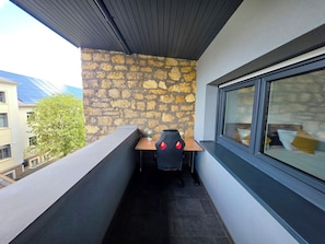Varanda com parede de pedra, mesa de madeira e cadeira preta com almofadas vermelhas.