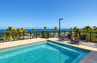 Piscina com vista para o oceano, palmeiras e espreguiçadeiras.