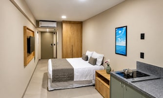 Quarto de hotel moderno com cama, televisão de tela plana, pintura, área de cozinha com fogão e guarda-roupa de madeira.