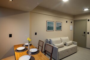 Uma área de refeições com uma mesa posta para dois, um sofá e duas imagens emolduradas na parede.