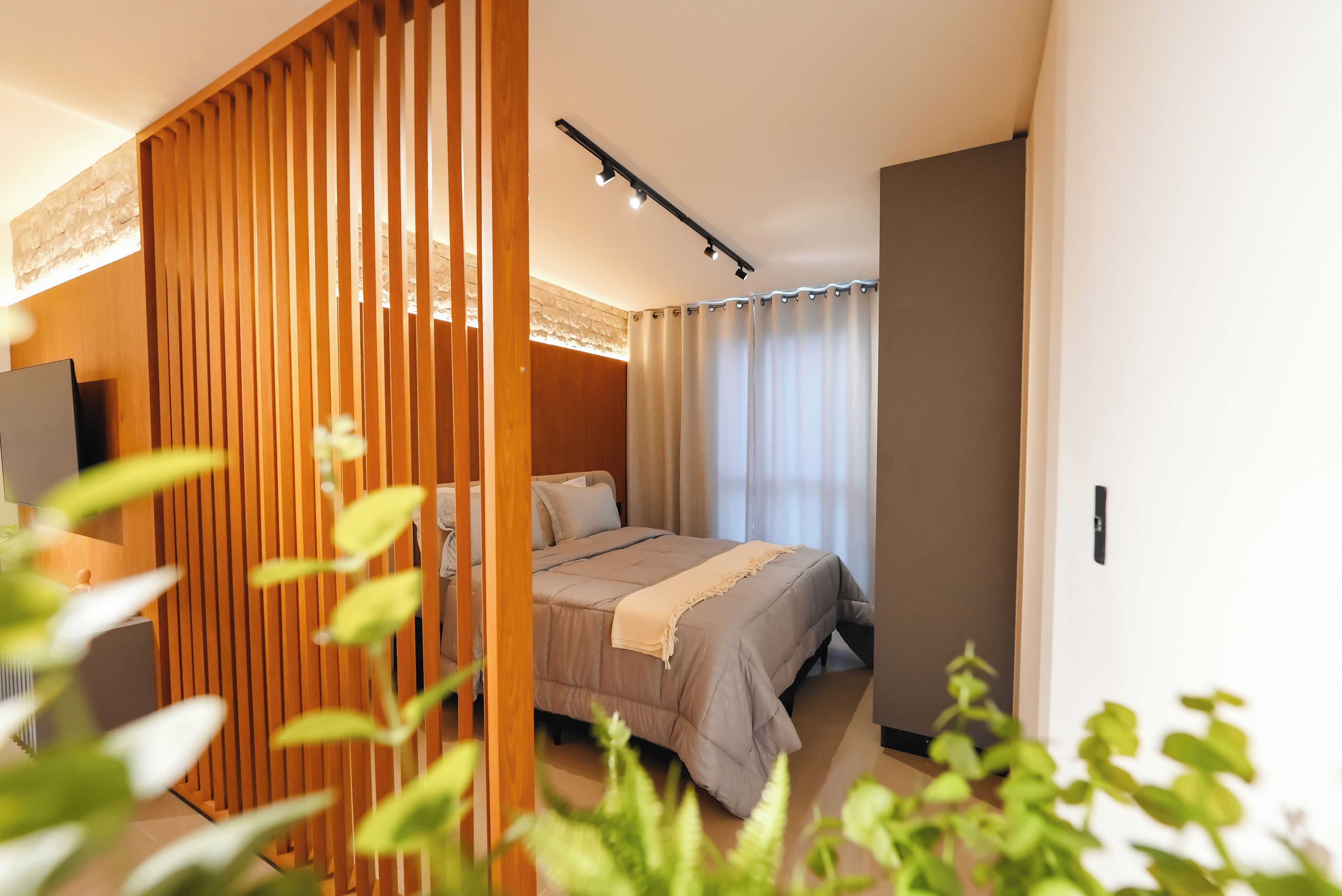 Quarto com cama, divisória de madeira e luminária no teto.