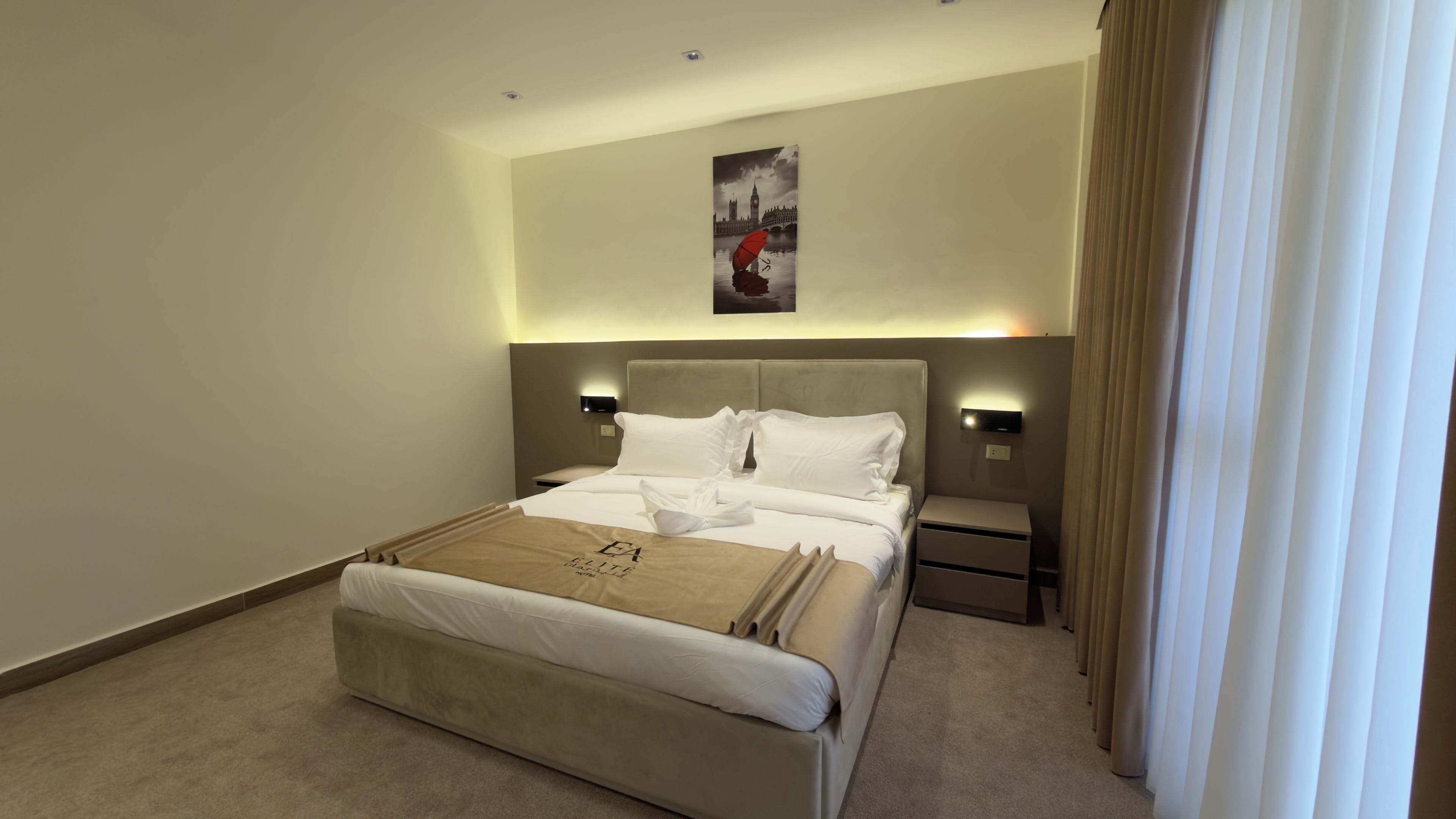 Quarto de hotel com cama, mesas de cabeceira, um quadro na parede e janela com cortinas.