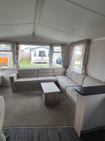 Interior de uma caravana com sofá modular, mesa pequena e janelas amplas.
