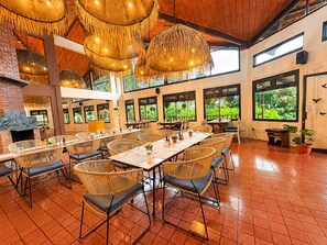 Uma sala de jantar espaçosa com pé direito alto, grandes janelas e muita luz natural.