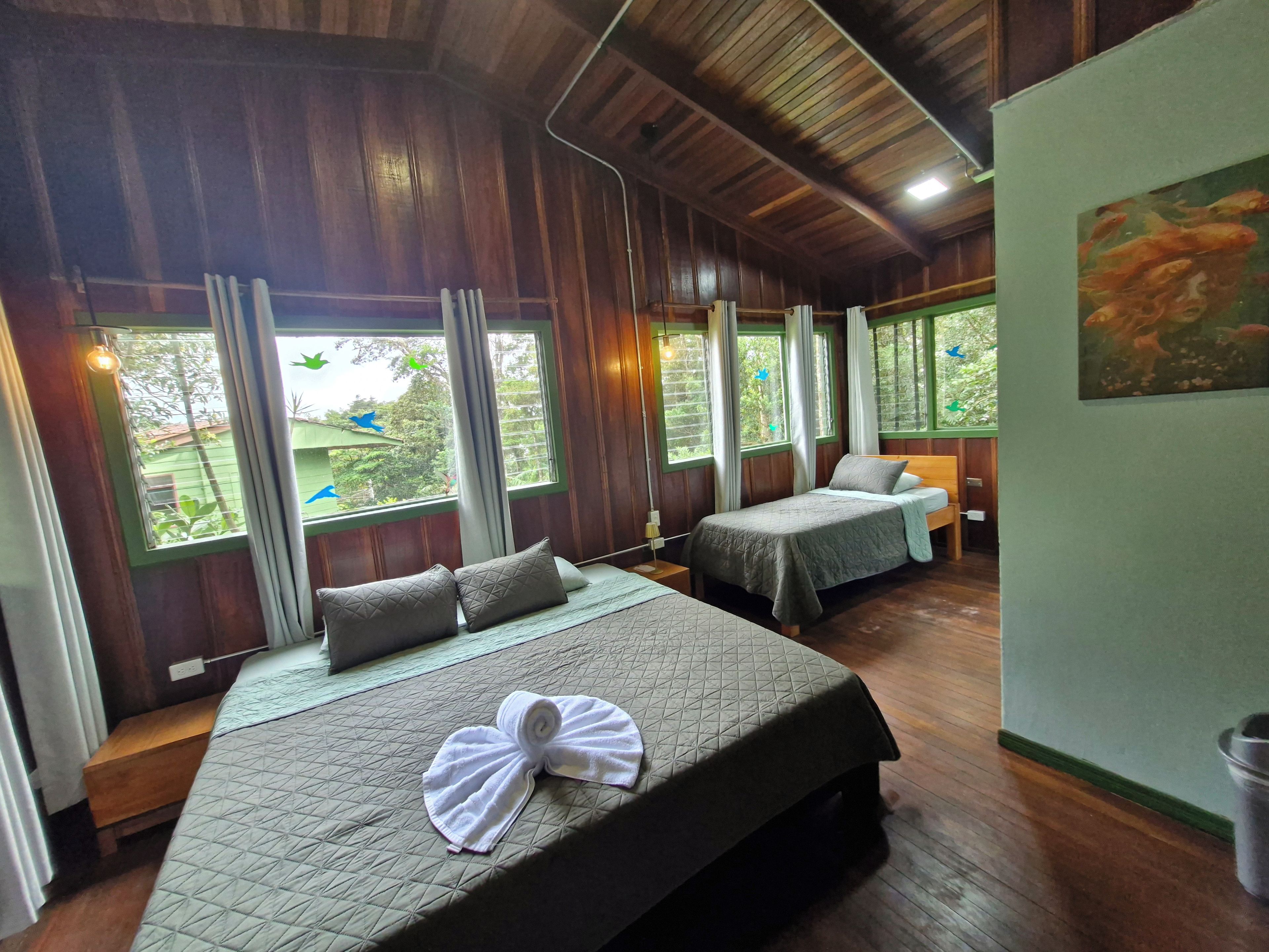 Quarto com duas camas, paredes de madeira, janelas amplas e um quadro.