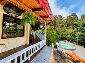 Área externa coberta com piscina, deck de madeira e plantas penduradas.