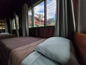 Quarto com cama, janela com cortinas e vista para prédios.