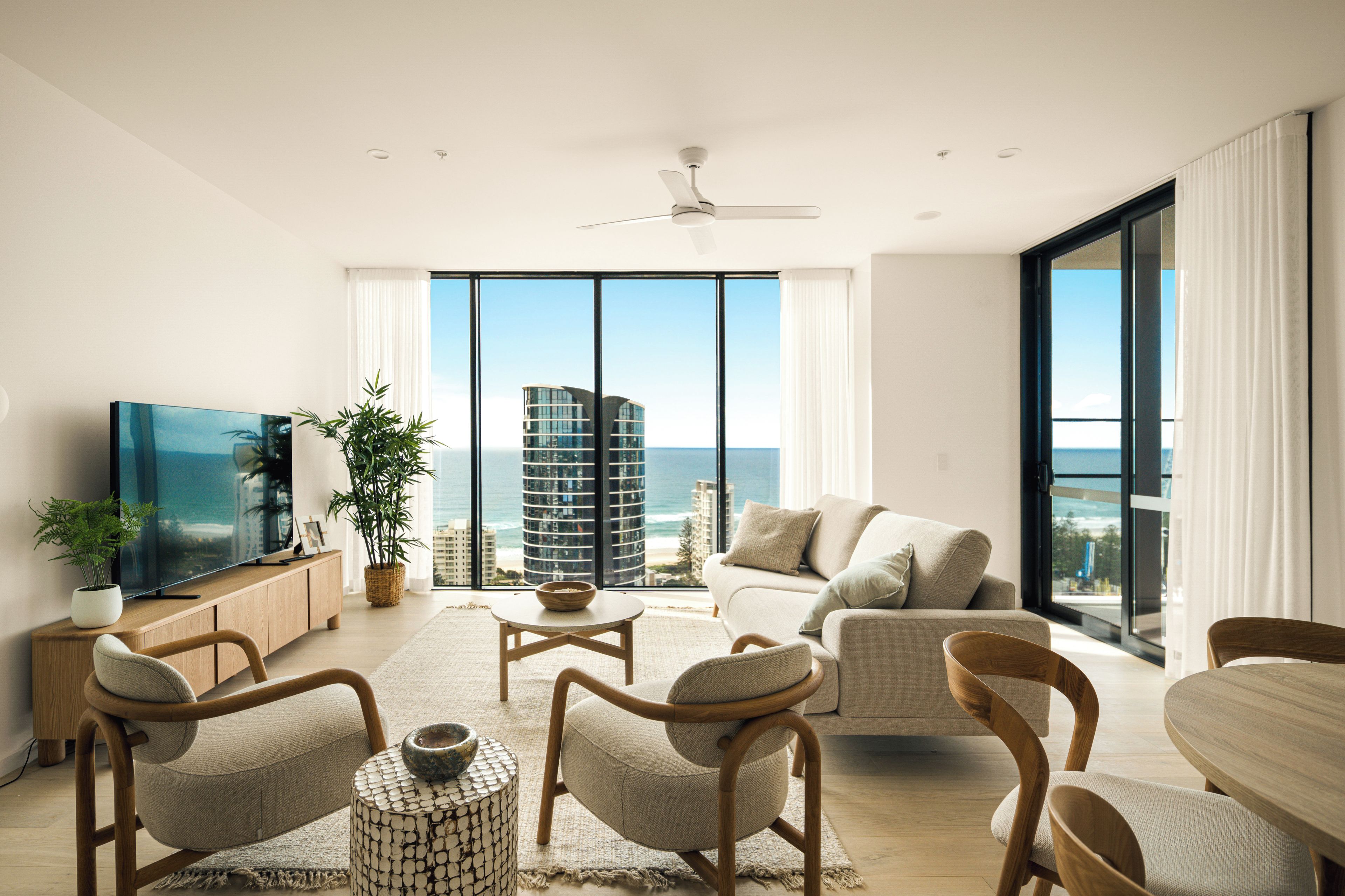 Uma sala de estar moderna com televisão, assentos, área de jantar e vista para o horizonte urbano através de grandes janelas.
