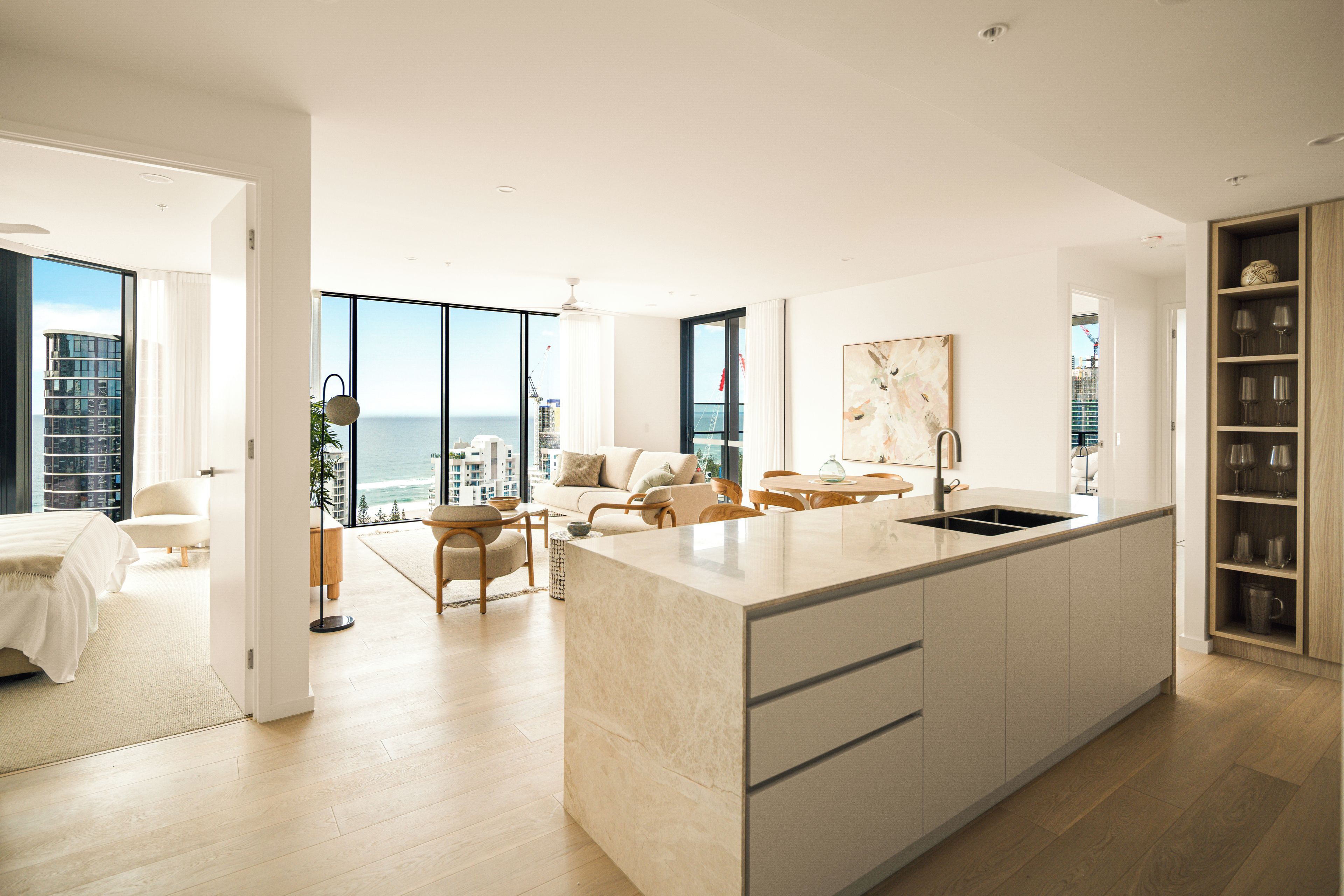Cozinha moderna com uma ilha grande, área de jantar com vista para o oceano e sala de estar com sofá e poltronas.