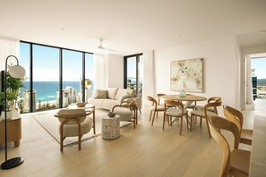 Uma sala de estar moderna com vista para o oceano, uma área de jantar com mobiliário de madeira e um grande quadro abstrato na parede.