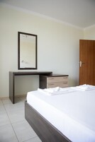 Quarto com cama, escrivaninha de madeira com gavetas, espelho e guarda-roupa.