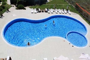 Uma piscina grande e de formato peculiar com design curvo, cercada por espreguiçadeiras e um deck pavimentado.