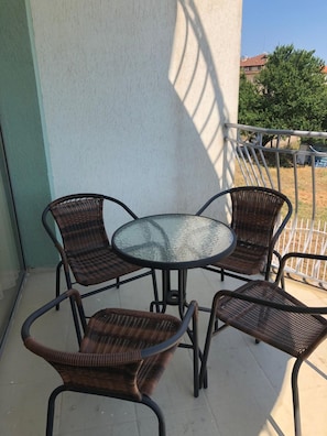 Varanda com mesa de vidro redonda e quatro cadeiras de vime.