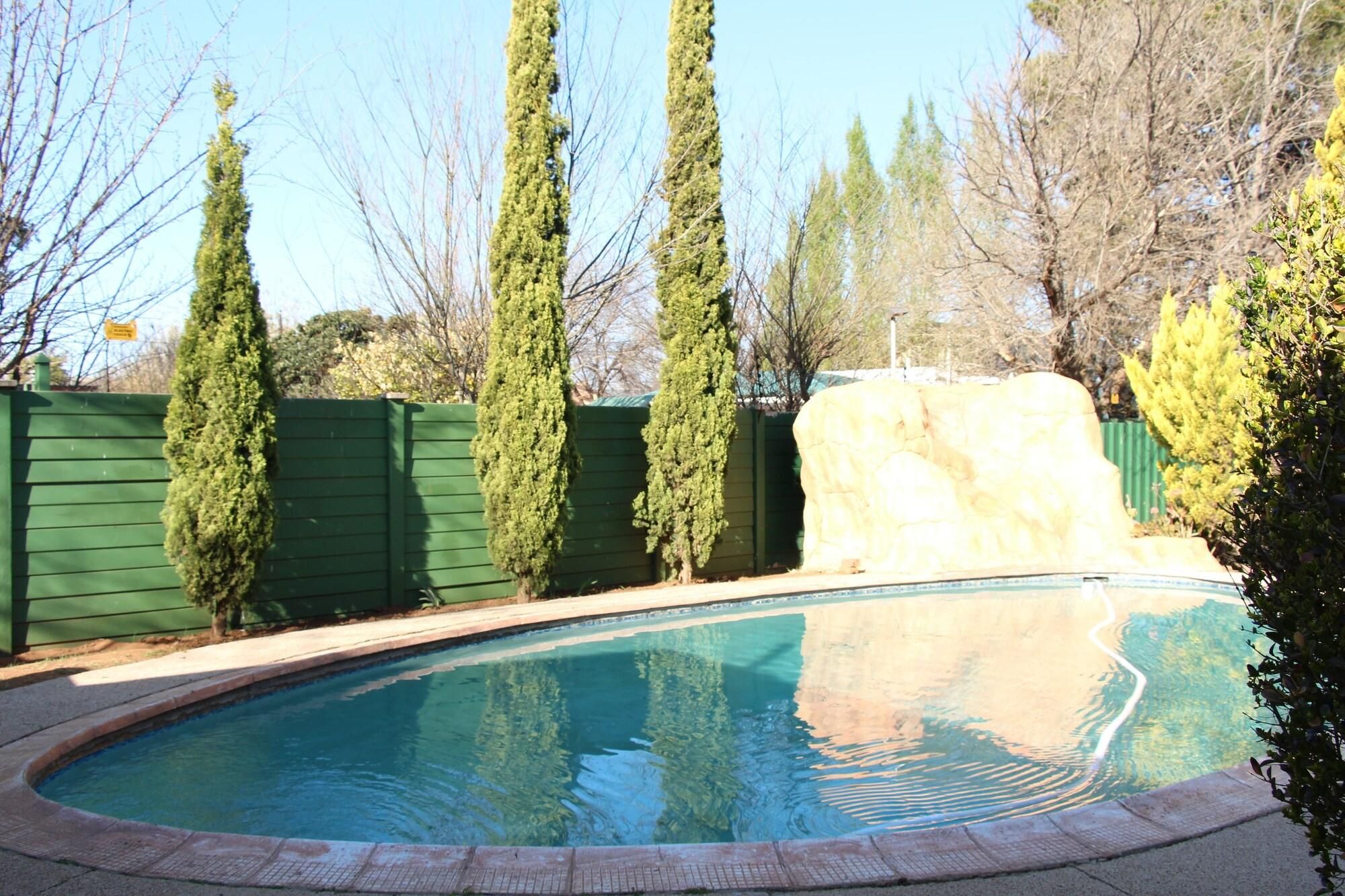 Piscina com muro de pedra e cerca verde.
