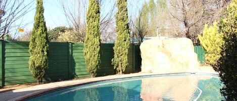 Piscina com muro de pedra e cerca verde.