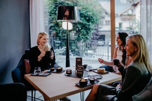 Um grupo de pessoas sentadas à mesa, com um cardápio, copos e uma vela, em um ambiente com uma janela grande e um abajur.