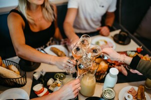 Um grupo de pessoas brindando com taças de champanhe em uma mesa com diversos alimentos e uma garrafa de leite.