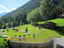 Paisagem montanhosa com área gramada, uma cabana de madeira e um muro de pedra.