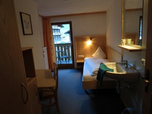Quarto de hotel com cama, escrivaninha, cadeira, banheiro com pia e varanda com vista.