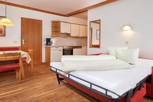 Quarto compacto com cama, escrivaninha, cozinha compacta e espelho.