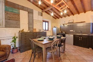Uma cozinha rústica com armários de madeira, uma mesa de jantar posta com pratos e copos, e um vaso com planta.
