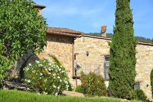 Edifício de pedra com telhado de azulejos, rodeado por vegetação e plantas floridas.