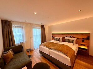 Quarto de hotel com uma cama grande, um sofá, uma mesa redonda pequena e vista para o exterior pelas janelas.